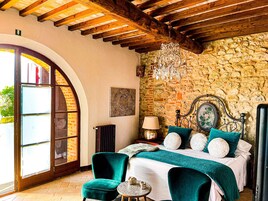 Quarto com parede de pedra, cama com roupa de cama verde-água, um candelabro e vista através de uma porta de vidro.
