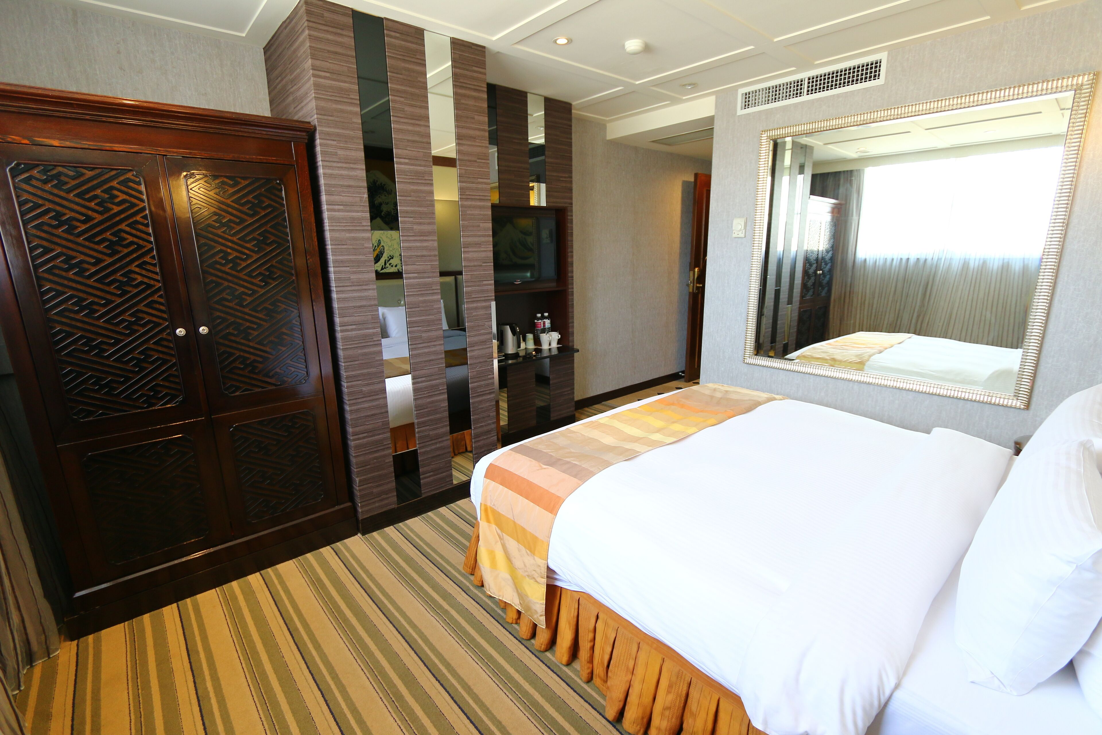 Quarto de hotel com uma cama grande, um guarda-roupa, um espelho e uma televisão.