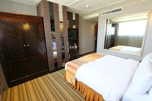 Quarto de hotel com uma cama grande, um guarda-roupa, um espelho e uma televisão.