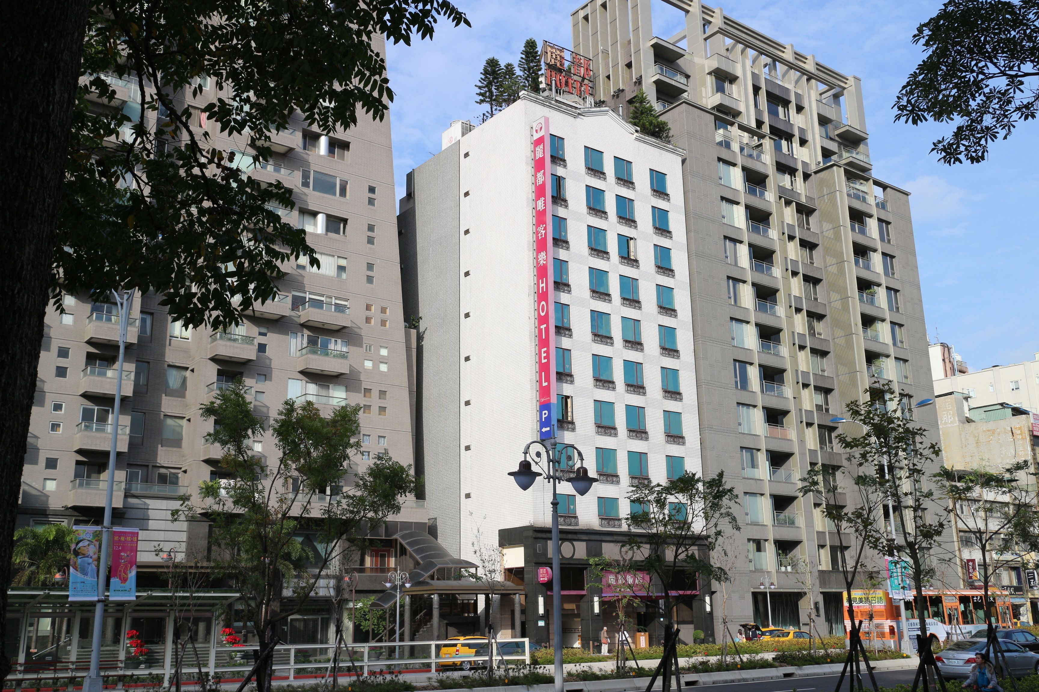 Um hotel com vários andares e uma placa vermelha vertical que destaca o nome e os serviços.