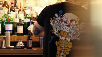Uma área de bar com diversos frascos e uma pessoa vestindo uma t-shirt estampada.