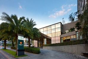 Um edifício moderno com fachada de vidro, palmeiras e uma placa indicando área de estacionamento.