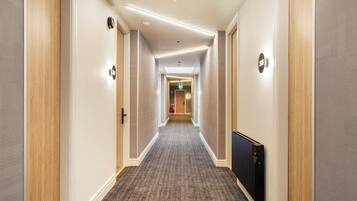 Corredor de hotel com piso carpetado, painéis de madeira nas paredes e um radiador à direita.