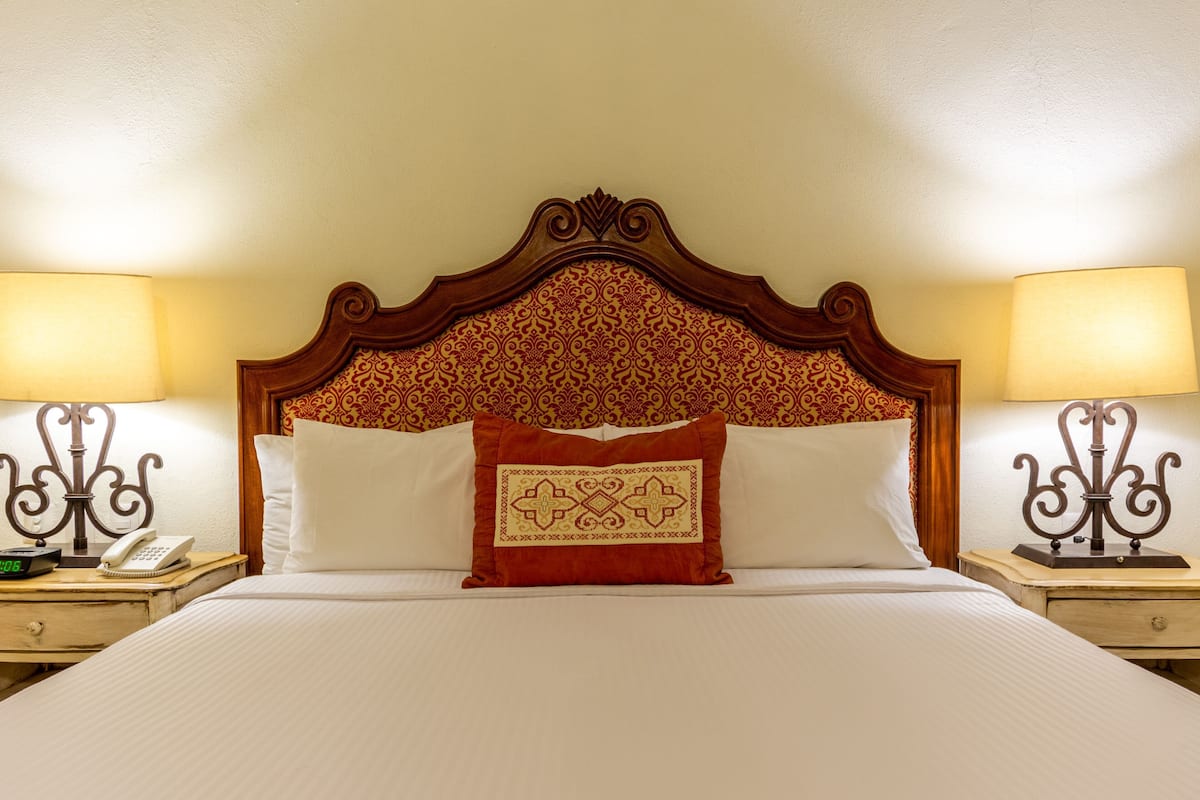 Quarto de hotel com uma cama grande, duas mesas de cabeceira, um painel de cabeceira decorativo e duas luminárias.