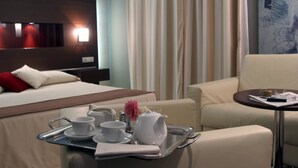Quarto de hotel com cama, sofá, uma pequena mesa com bandeja de itens de café da manhã e um quadro na parede.