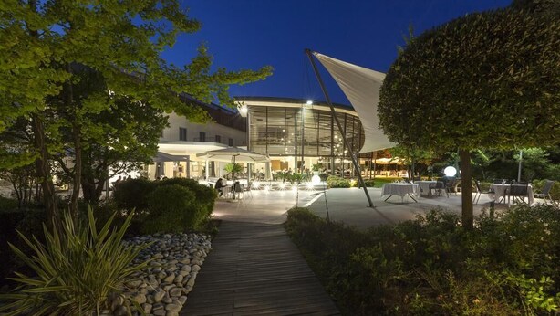 Um hotel moderno com um caminho de madeira que leva a uma área de refeições coberta ao ar livre.