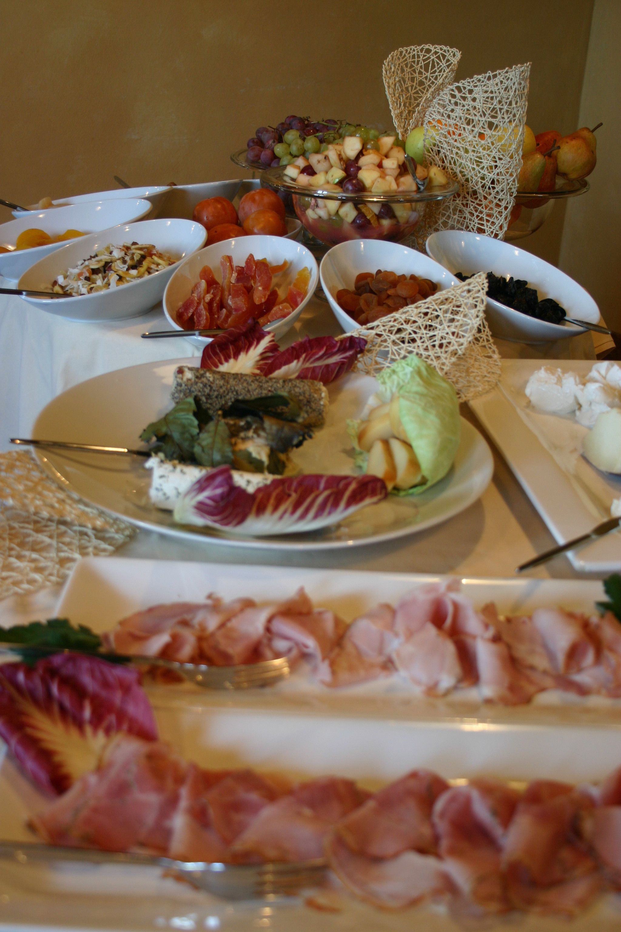 Mesa de buffet com diversos alimentos, incluindo frutas, queijos e carnes.