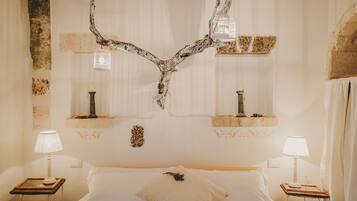 Quarto com uma cama grande, duas mesas de cabeceira com luminárias, um painel decorativo de galhos na parede e uma janela com cortinas.
