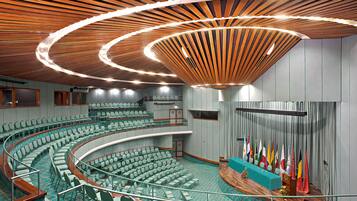 Uma sala de conferências com assentos em diferentes níveis, um pódio com bandeiras e um design de teto moderno.