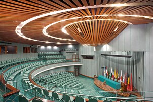 Uma sala de conferências com assentos em diferentes níveis, um pódio com bandeiras e um design de teto moderno.