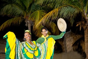 Duas pessoas em trajes típicos, com uma palmeira e uma cascata ao fundo.