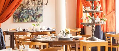 Uma sala de jantar com várias mesas e cadeiras de madeira, um candelabro e um suporte escalonado com xícaras e flores.