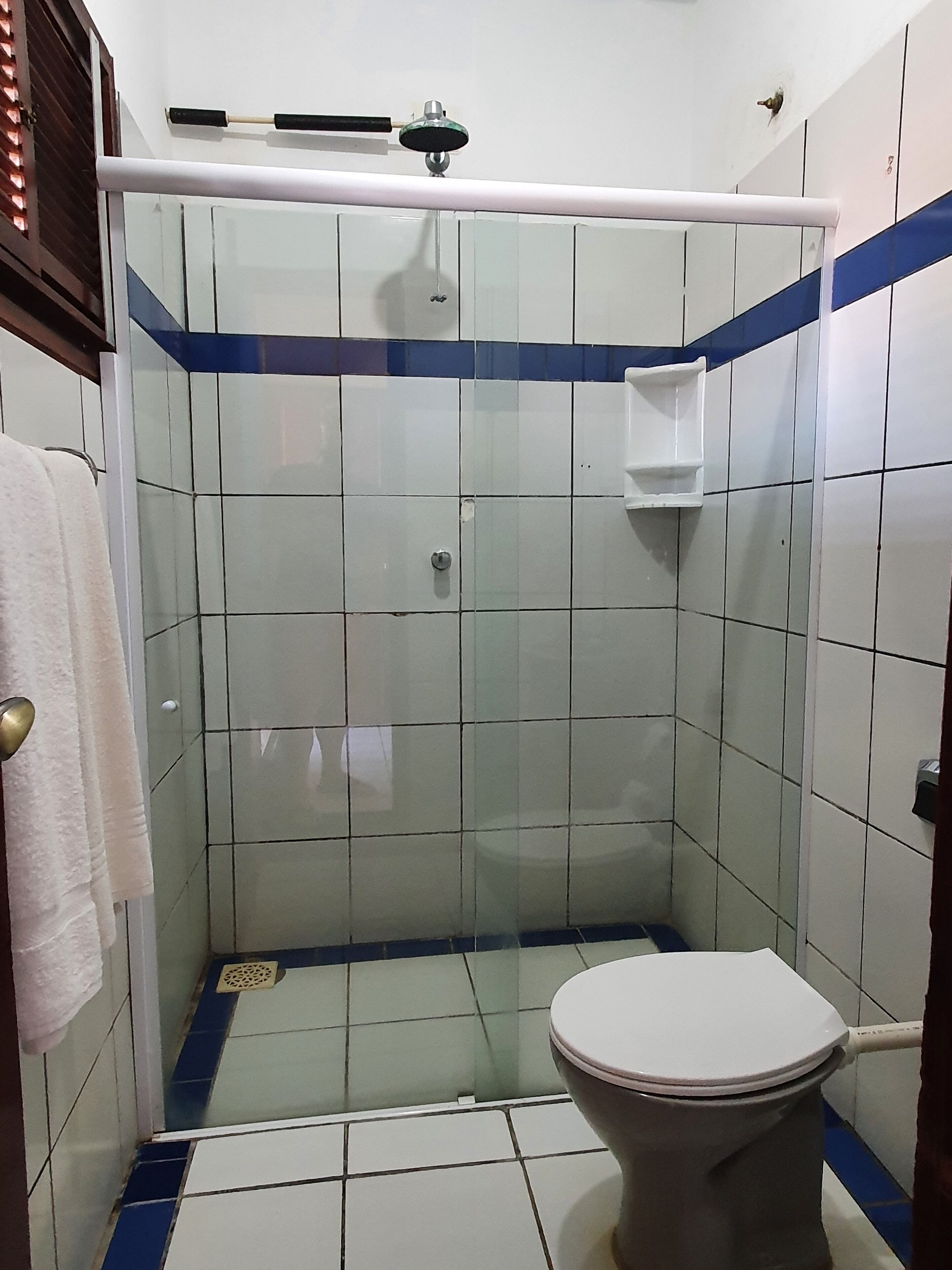 Uma casa de banho pequena com sanita, chuveiro com porta de vidro e toalha pendurada na parede.