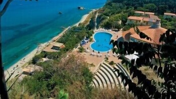 Um resort com uma piscina grande, praia e vegetação exuberante.
