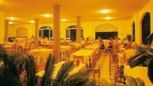 Uma área de refeições com mesas e cadeiras, pilares grandes e portas em arco.
