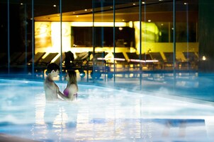 Uma piscina interior com paredes de vidro transparente, espreguiçadeiras e iluminação agradável.