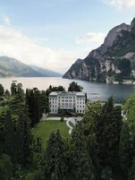 Um edifício grande e branco com fachada simétrica, rodeado por vegetação exuberante e um lago.