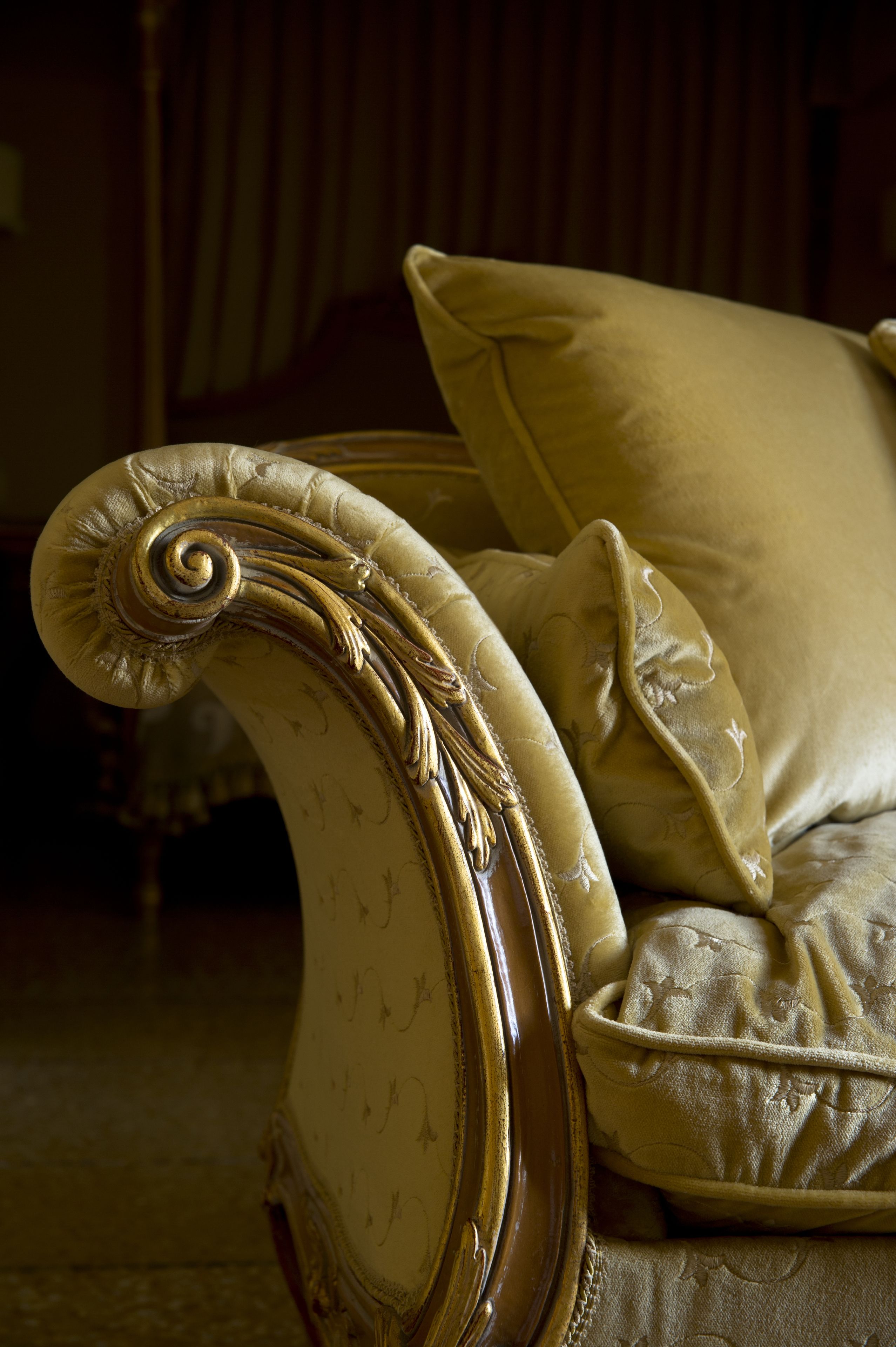 Um close-up de um sofá em estilo vintage com encosto curvo e padrões decorativos, acompanhado de uma almofada combinando.