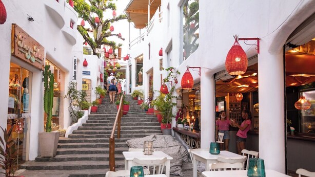 Uma rua estreita com escadas que levam a um restaurante, cercada por edifícios brancos e lanternas vermelhas.