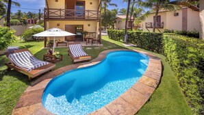 Piscina rodeada por espreguiçadeiras e um terraço com vista para um edifício amarelo e palmeiras.