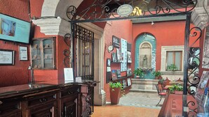Um saguão de hotel com uma parede vermelha, um balcão de recepção de madeira, uma vitrine de vidro e um piso de azulejos.