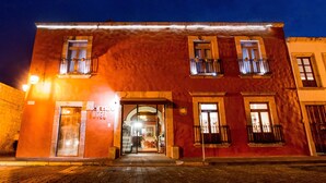 Um hotel com fachada vermelha, várias janelas e sacadas, e uma rua de paralelepípedos na frente.