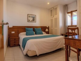 Quarto com cama de madeira, mesa de cabeceira, escrivaninha e janela com persianas.