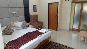 Quarto de hotel com cama, cadeira, guarda-roupa e uma pequena mesa.