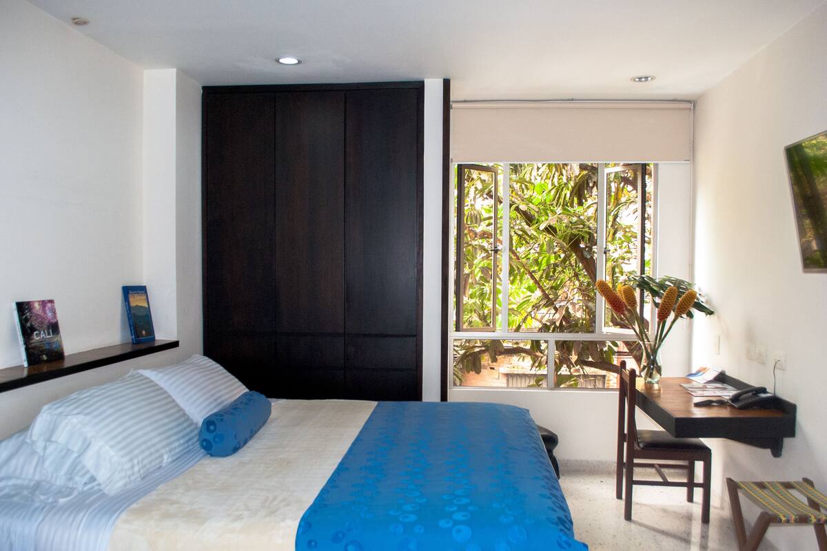 Quarto com cama, escrivaninha e janela com vista para o verde.