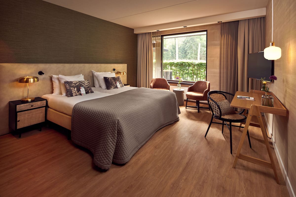Quarto de hotel moderno com uma cama grande, uma escrivaninha, uma cadeira e uma televisão.