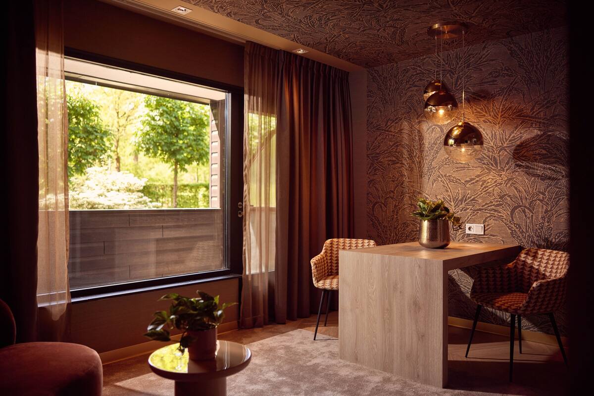 Quarto moderno com uma grande janela, uma mesa de jantar de madeira, duas cadeiras estampadas e um vaso com planta.