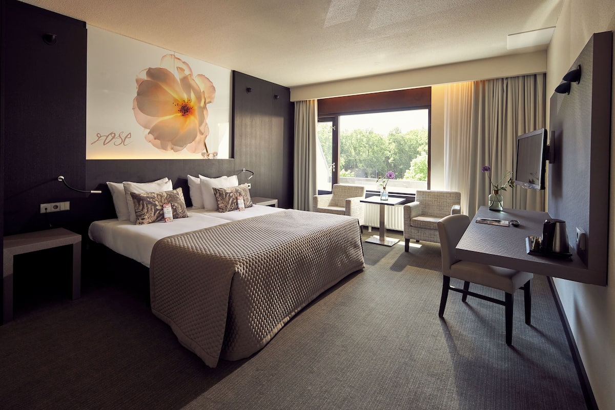 Quarto de hotel moderno com uma cama grande, uma escrivaninha, uma cadeira e vista para o exterior.
