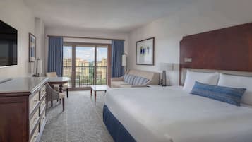 Quarto de hotel com cama grande, escrivaninha, cadeira, mesa pequena e varanda com vista para a cidade.