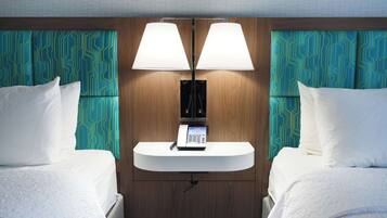 Quarto de hotel com duas camas, uma mesa de cabeceira com telefone e uma luminária na parede.