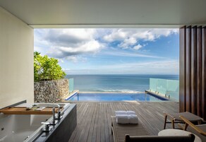 Varanda com vista para o oceano, deck de madeira, banheira e área de estar com toalhas.