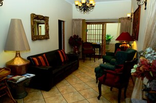 Uma sala de estar com sofá, poltronas, luminária, espelho e área de jantar com mesa e cadeiras.