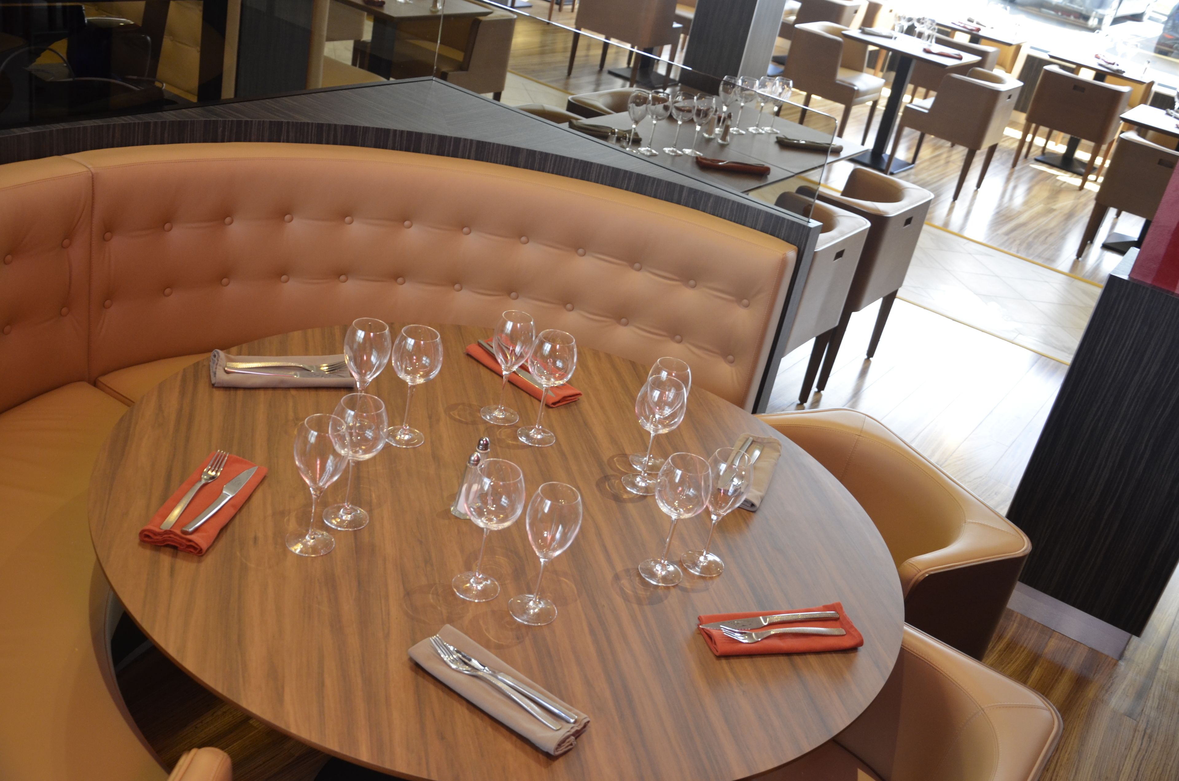 Mesa redonda com vários copos de vinho e talheres, rodeada por assentos acolchoados em um restaurante moderno.