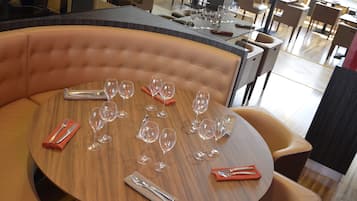 Mesa redonda com vários copos de vinho e talheres, rodeada por assentos acolchoados em um restaurante moderno.