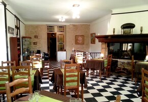 Uma sala de jantar com piso xadrez, cadeiras de madeira e mesas postas.