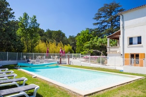 Piscina com espreguiçadeiras, área de estar coberta e um edifício com varanda.