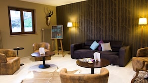 Um quarto com sofá, poltronas, uma mesa pequena, um quadro em cavalete e uma janela grande.