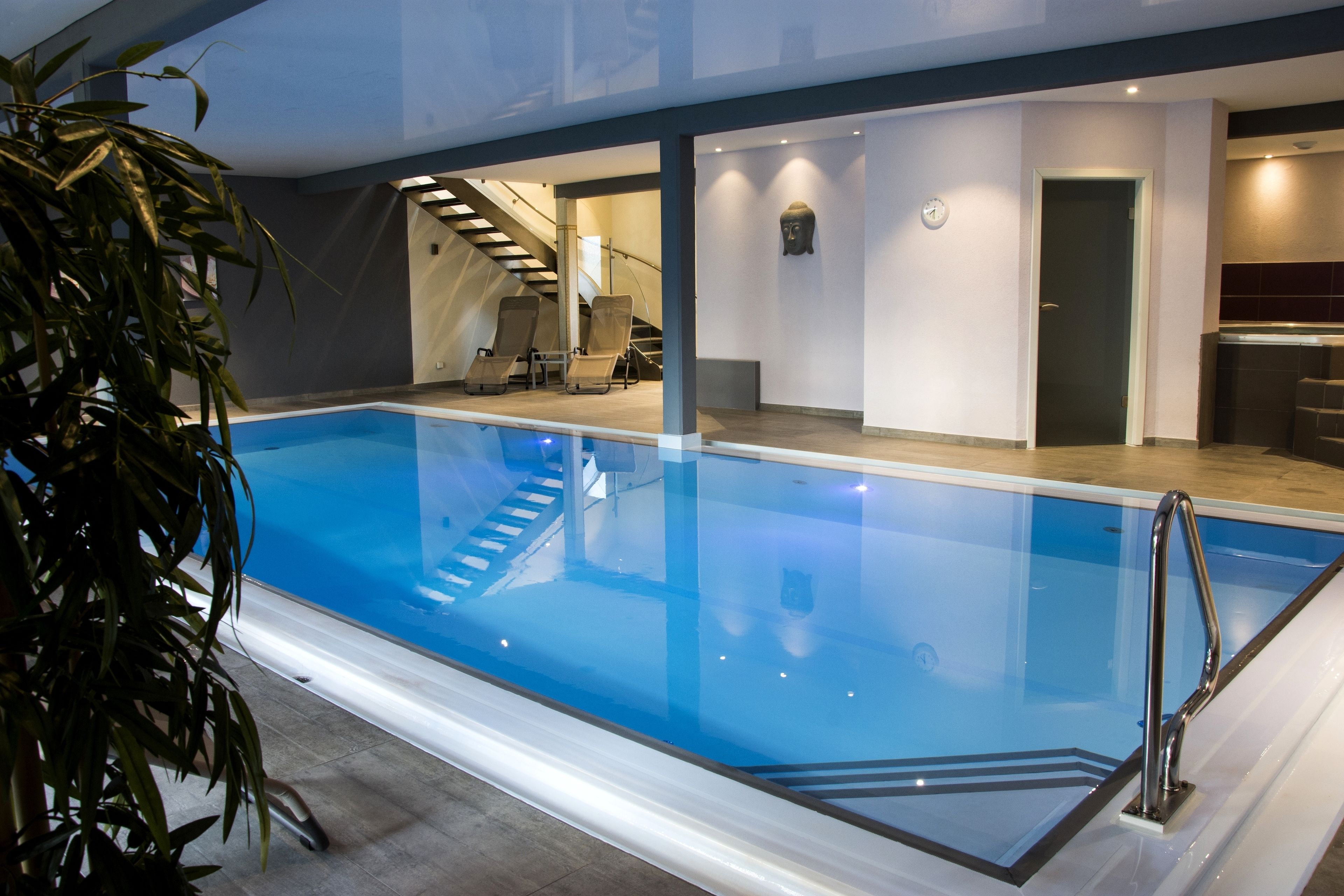 Piscina interior moderna com água cristalina, escadaria para um andar superior e design de interiores minimalista.