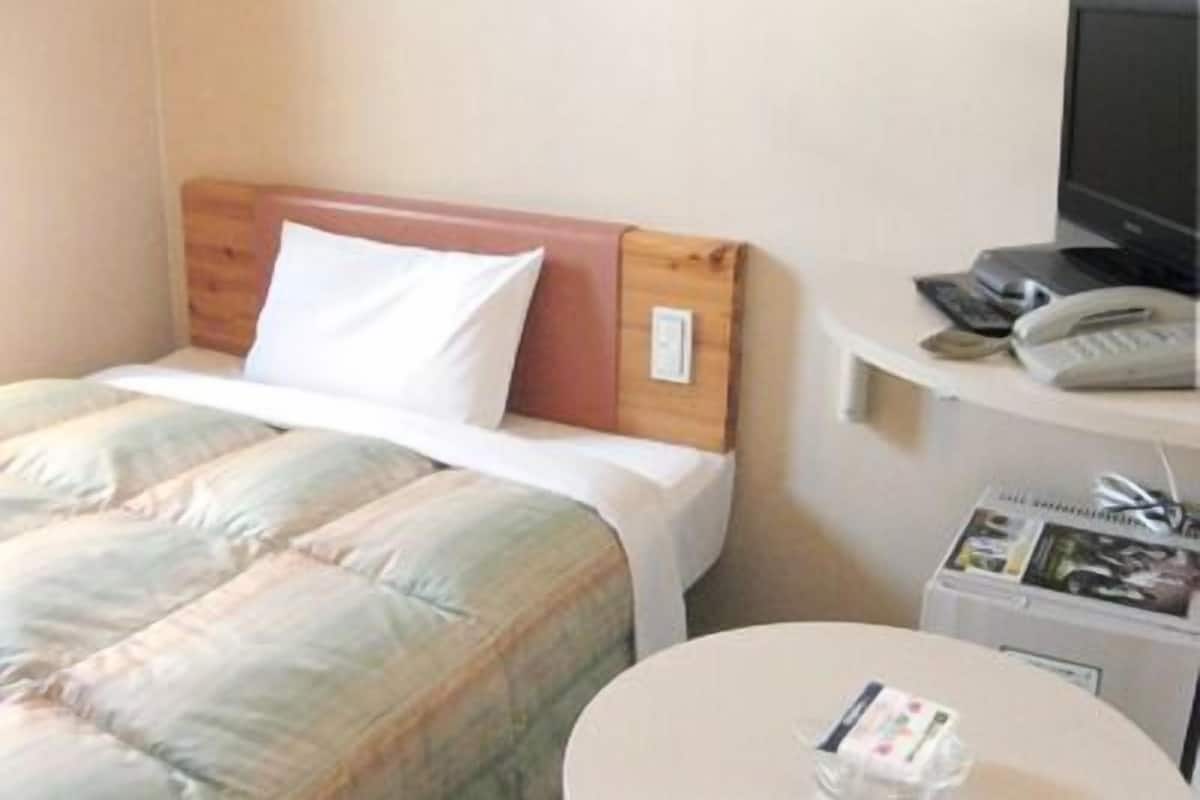 Quarto de hotel com cama, televisão, escrivaninha com telefone e uma pequena mesa com uma revista.
