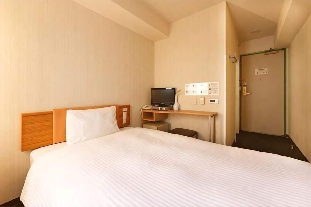 Quarto de hotel com cama, escrivaninha e computador, e uma televisão.