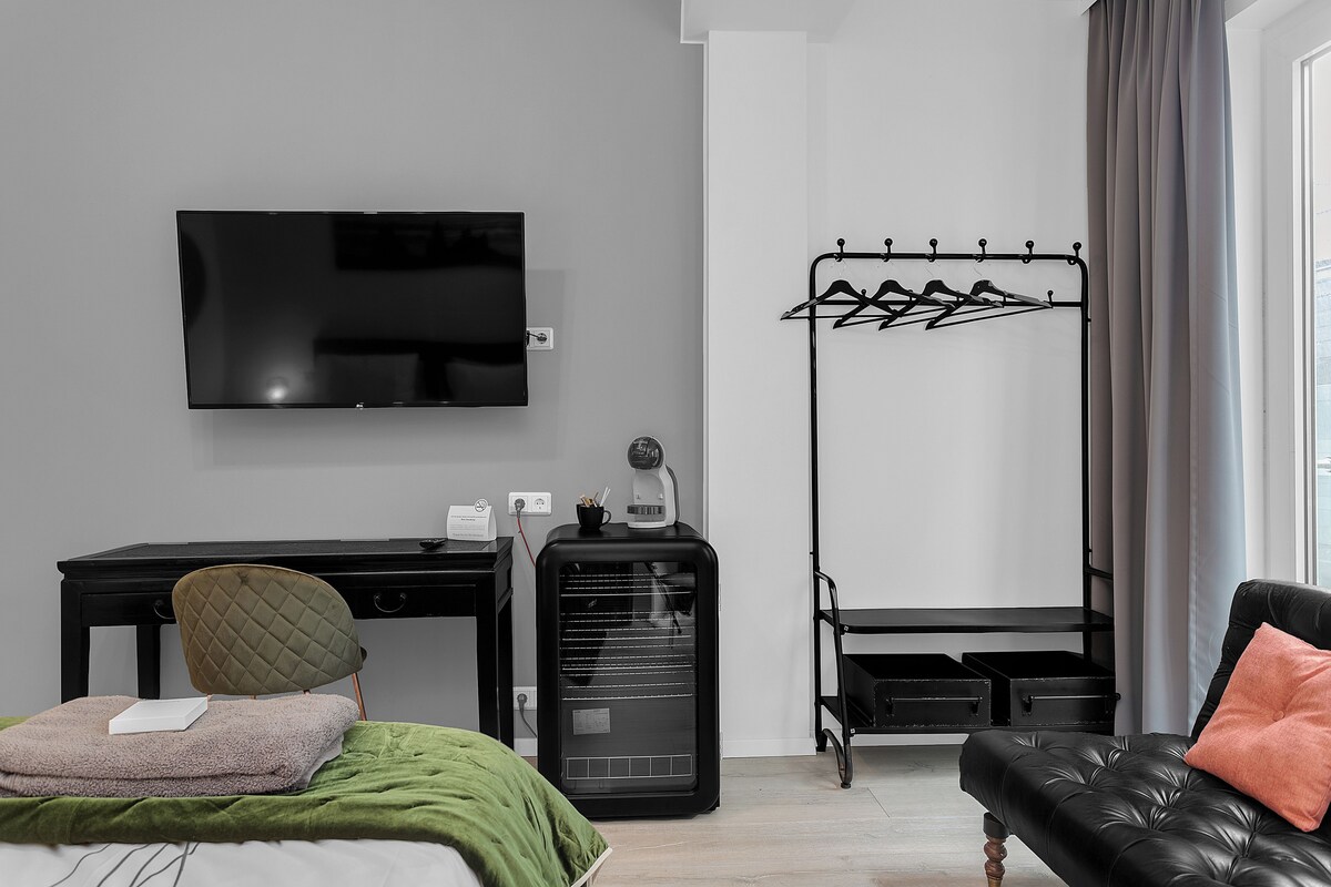 Quarto de hotel moderno com cama, escrivaninha, televisão, aquecedor, cabideiro e sofá de couro.