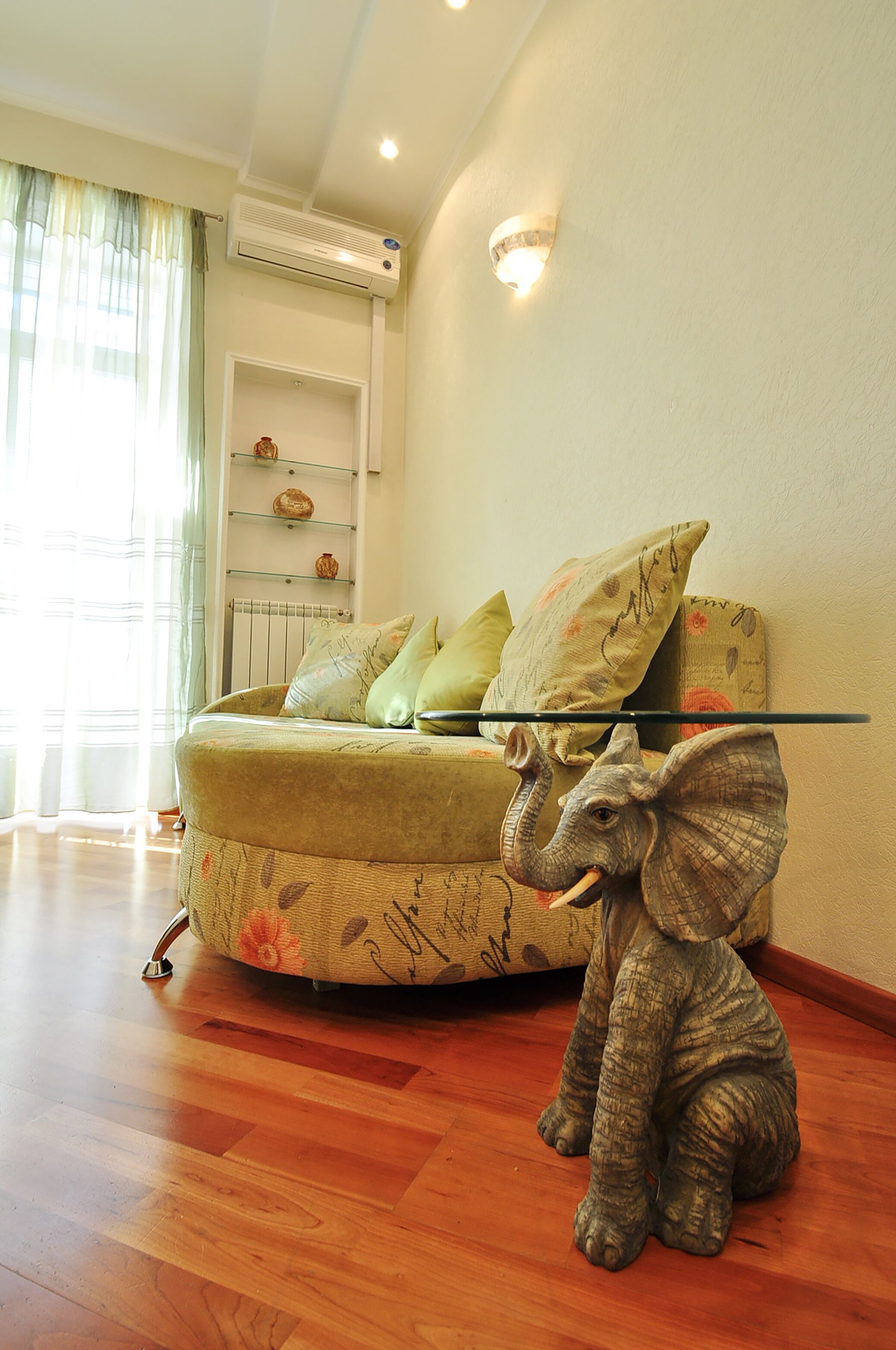Uma sala de estar com sofá, almofadas decorativas, mesa de centro de vidro e uma estátua de elefante.