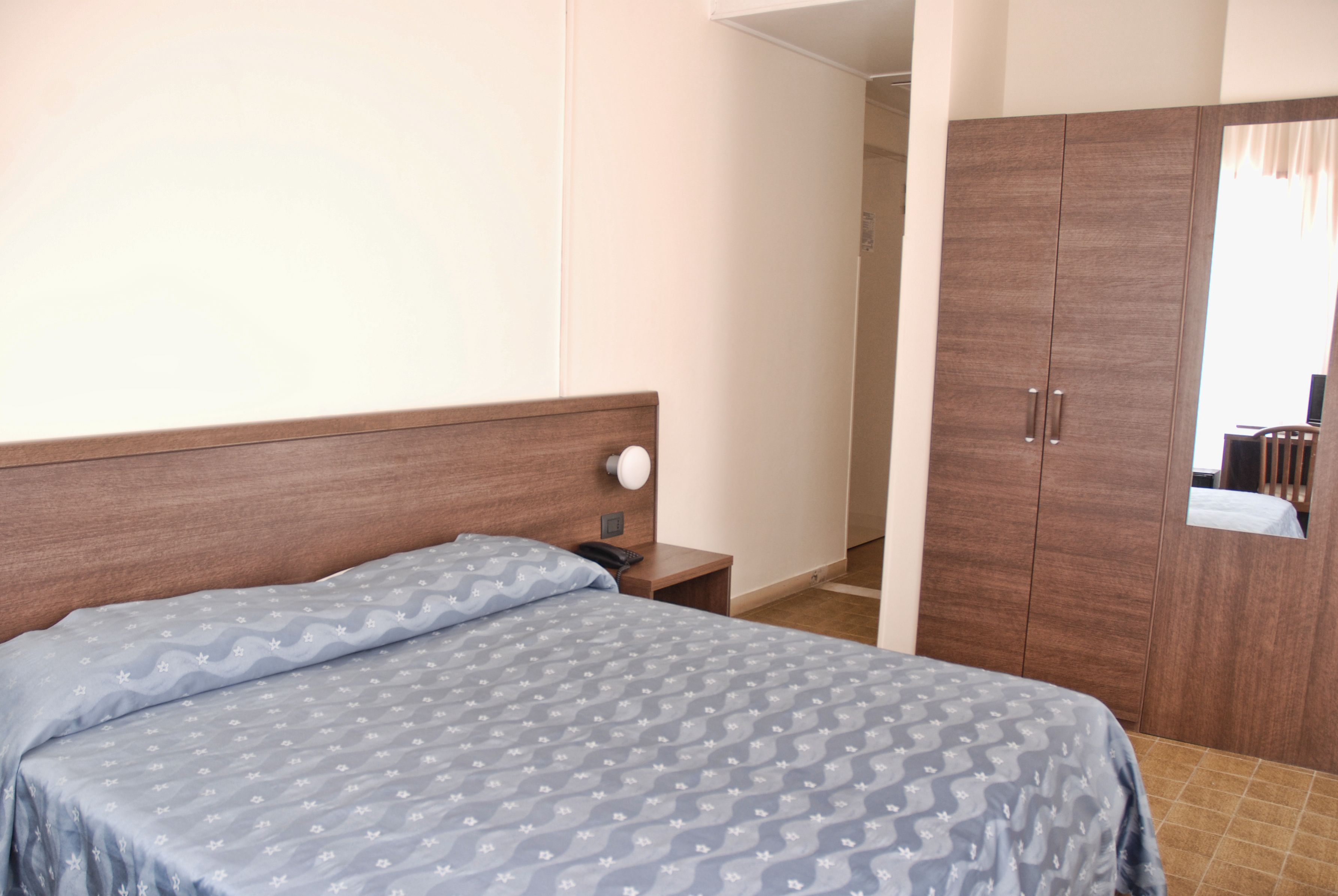 Quarto com cama, mesa de cabeceira, guarda-roupa e um pequeno espelho.
