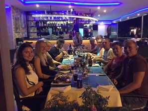 Um grupo de pessoas sentado à volta de uma mesa num restaurante, com um bar ao fundo.