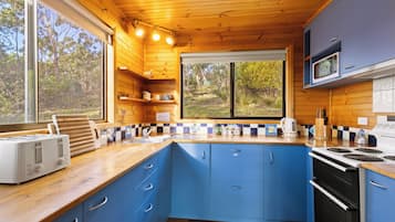 Cozinha compacta com armários de madeira, micro-ondas, fogão e janela com vista para a paisagem natural.