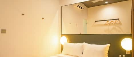 Quarto de hotel com cama, ventoinha no teto, espelho e mesa de cabeceira com luminária.